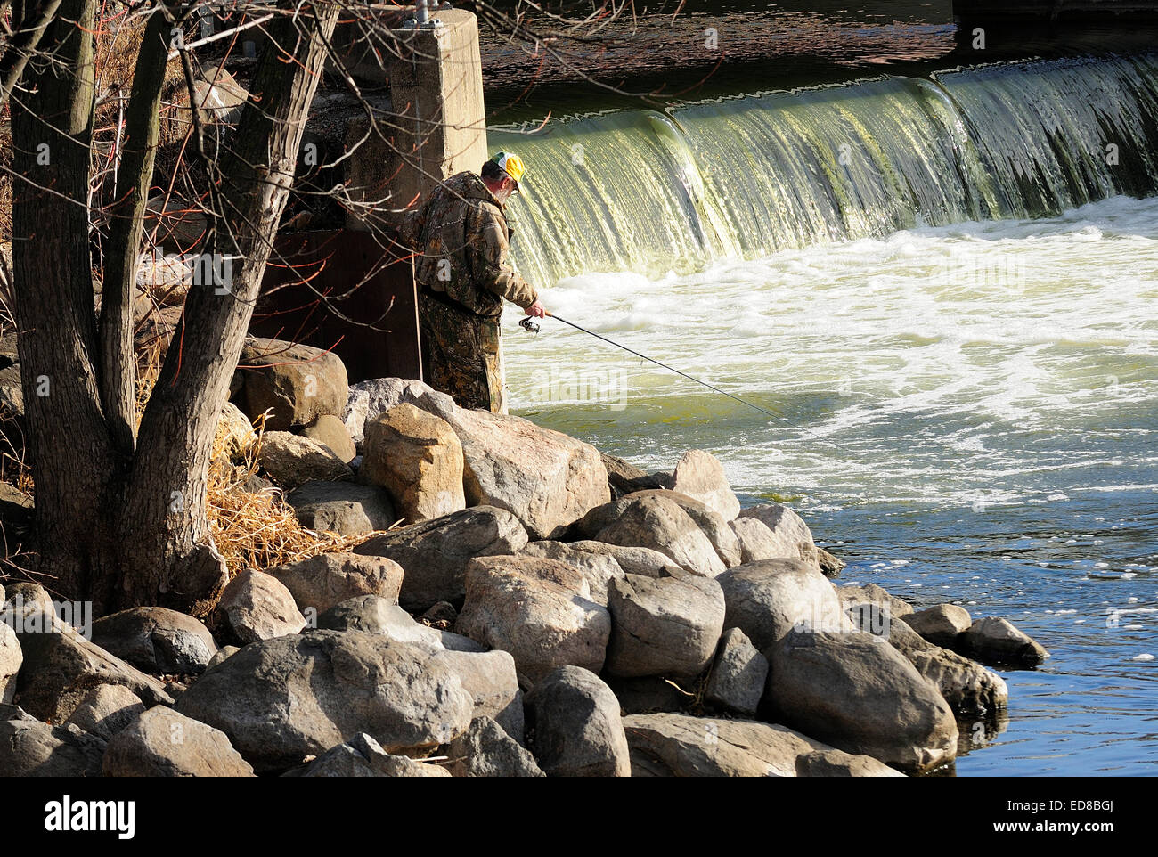 Lone fisherman fishing from shoreline near river dam Stock Photo - Alamy
