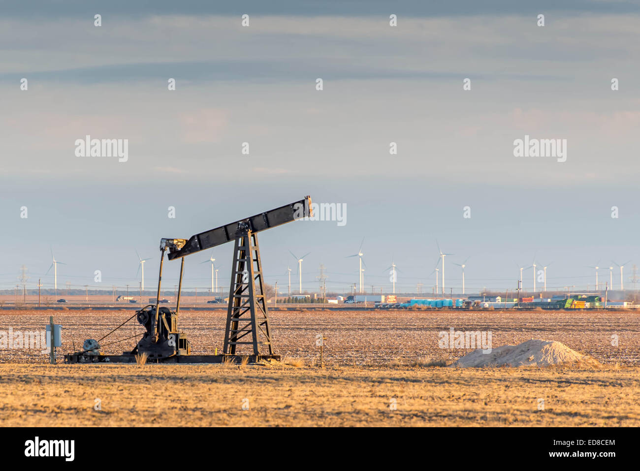 old oil derrick in a golden field with wind turbines in background ...