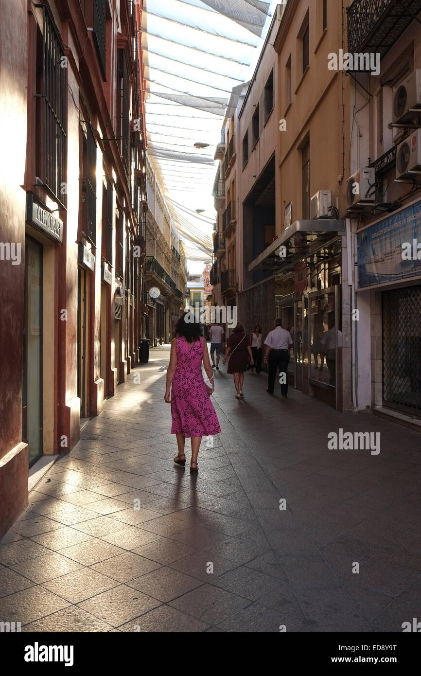 Seville Spain: Women in pink dress walking along shaded shopping street ...