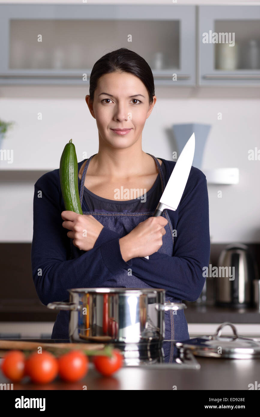 Happy young woman posing in her kitchen with her arms crossed holding a ...
