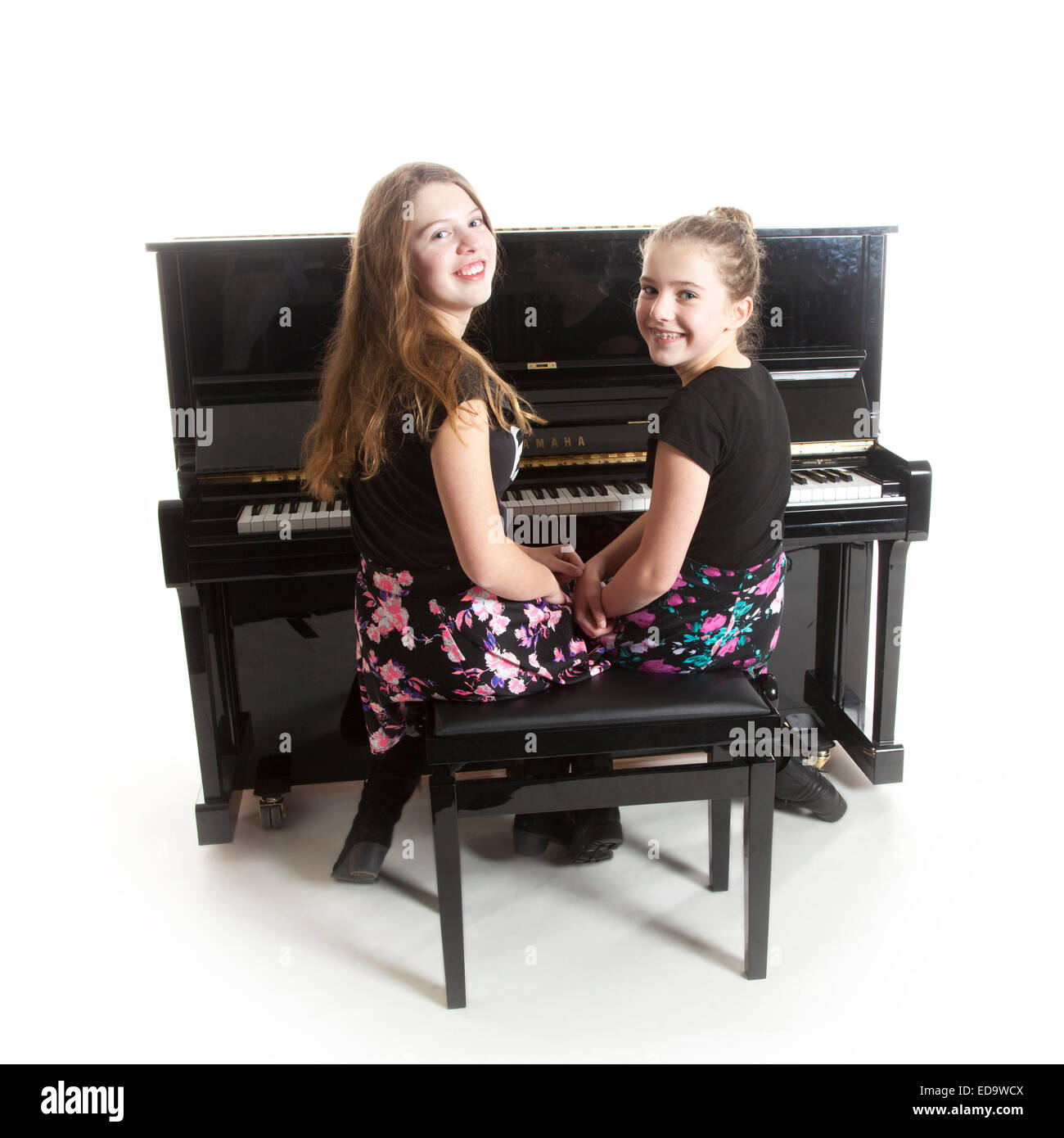 two teenage girls and black upright piano in studio against white ...