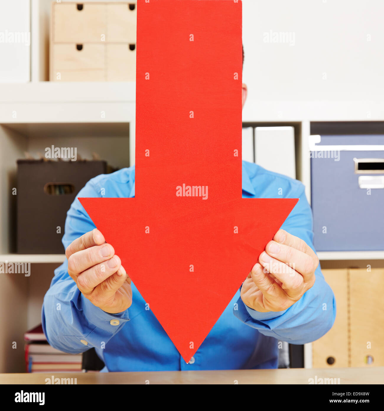 Business man holding big red arrow down in office Stock Photo - Alamy