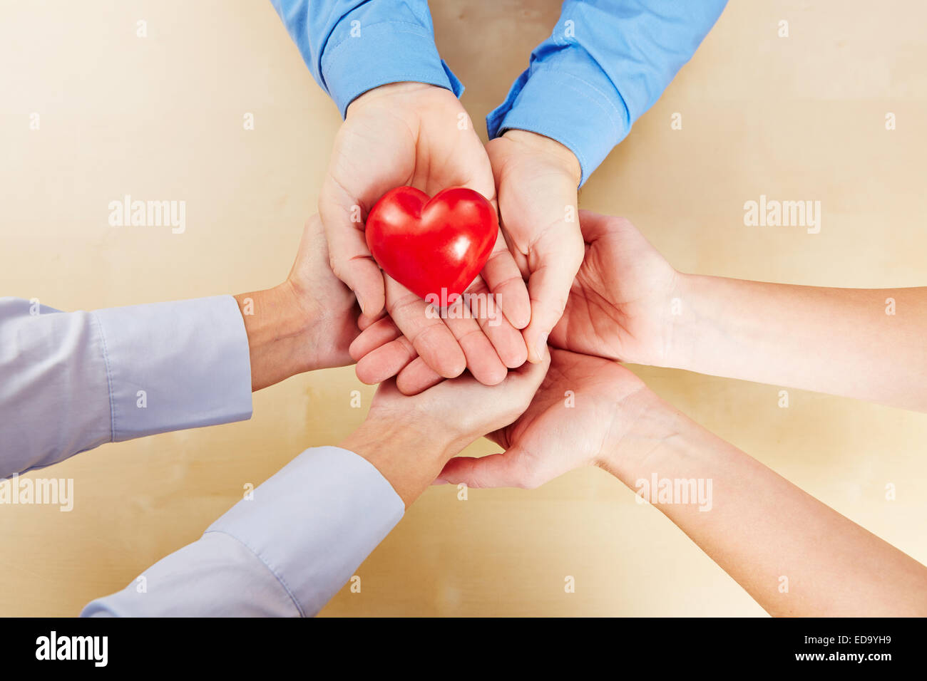 Many hands holding together a little red heart Stock Photo - Alamy