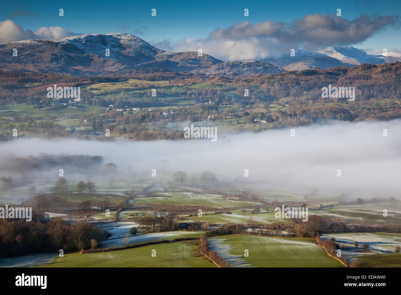 Snow-capped Wetherlam and Bowfell, with low mist above Outgate, near ...