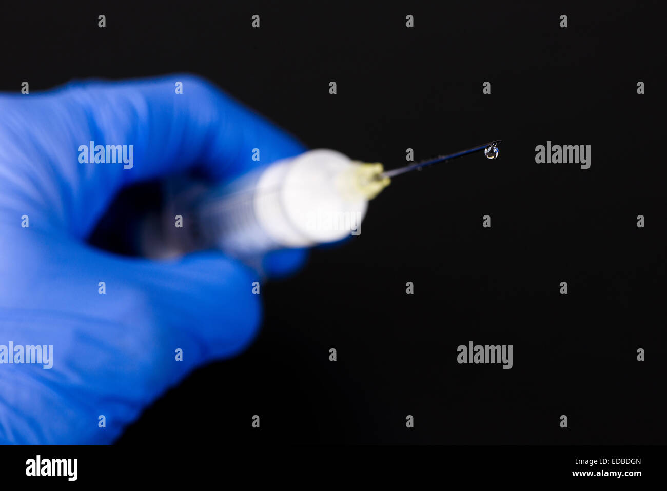 A hand with a blue medical glove is holding a syringe with a hypodermic ...