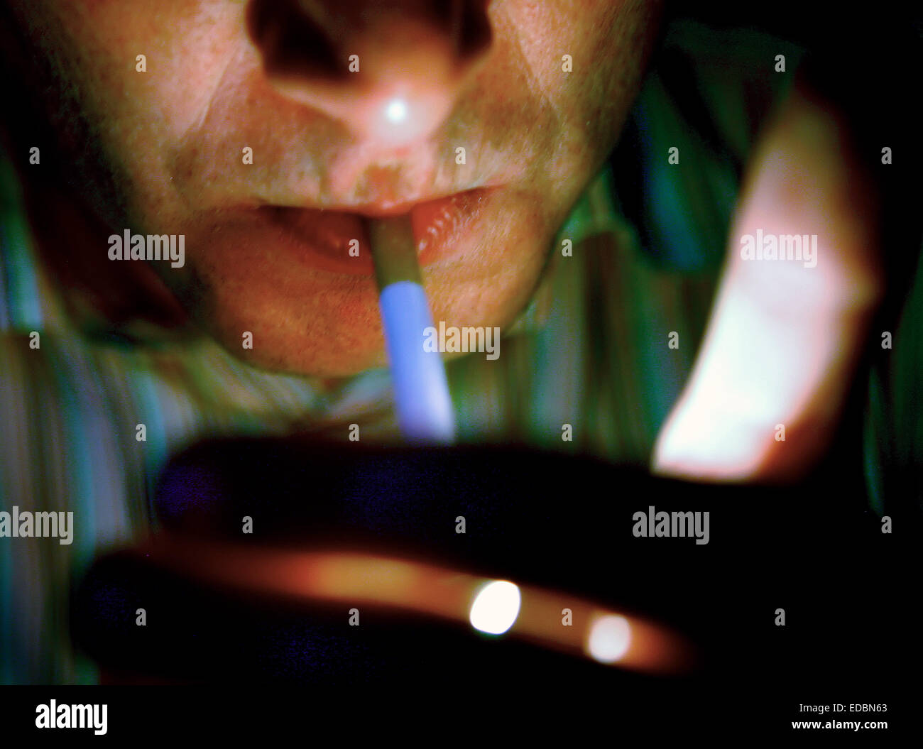 A close-up picture of a man lighting a cigarette, his face solely lit ...