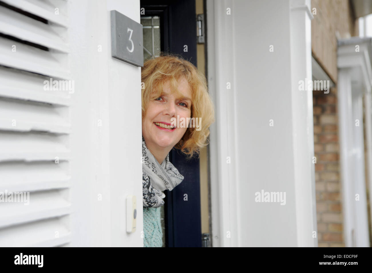 Woman looking out of her front door to greet visitors Stock Photo - Alamy