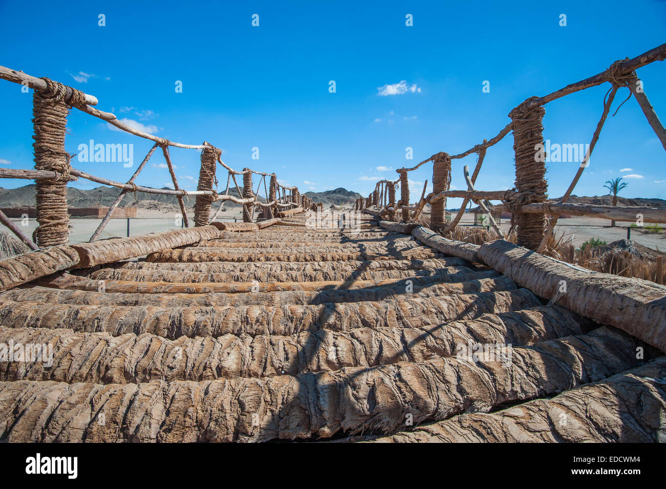 Wooden log rope bridge across a remote desert landscape with blue sky ...