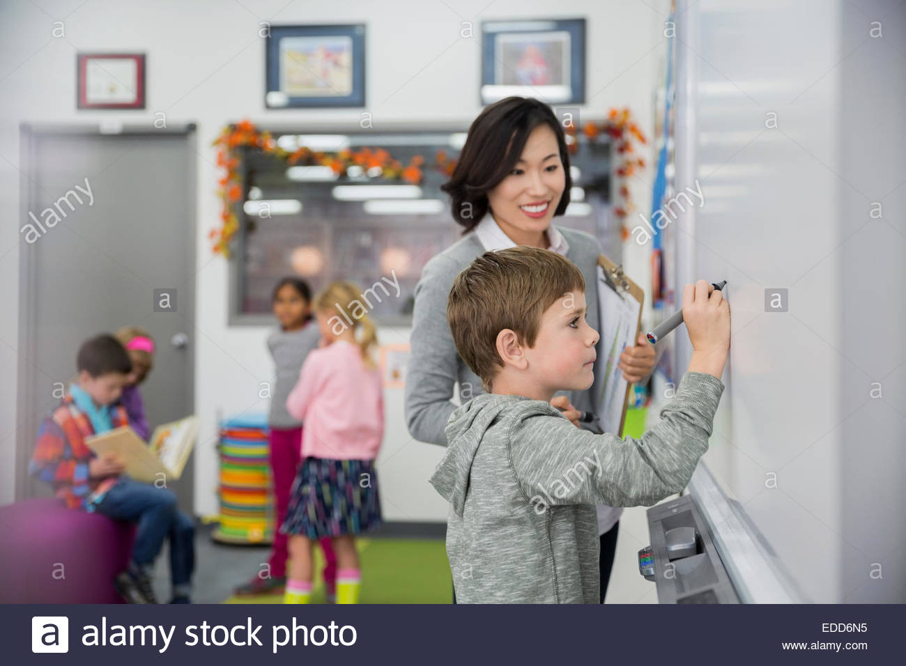 Teacher watching elementary student writing at whiteboard Stock Photo ...