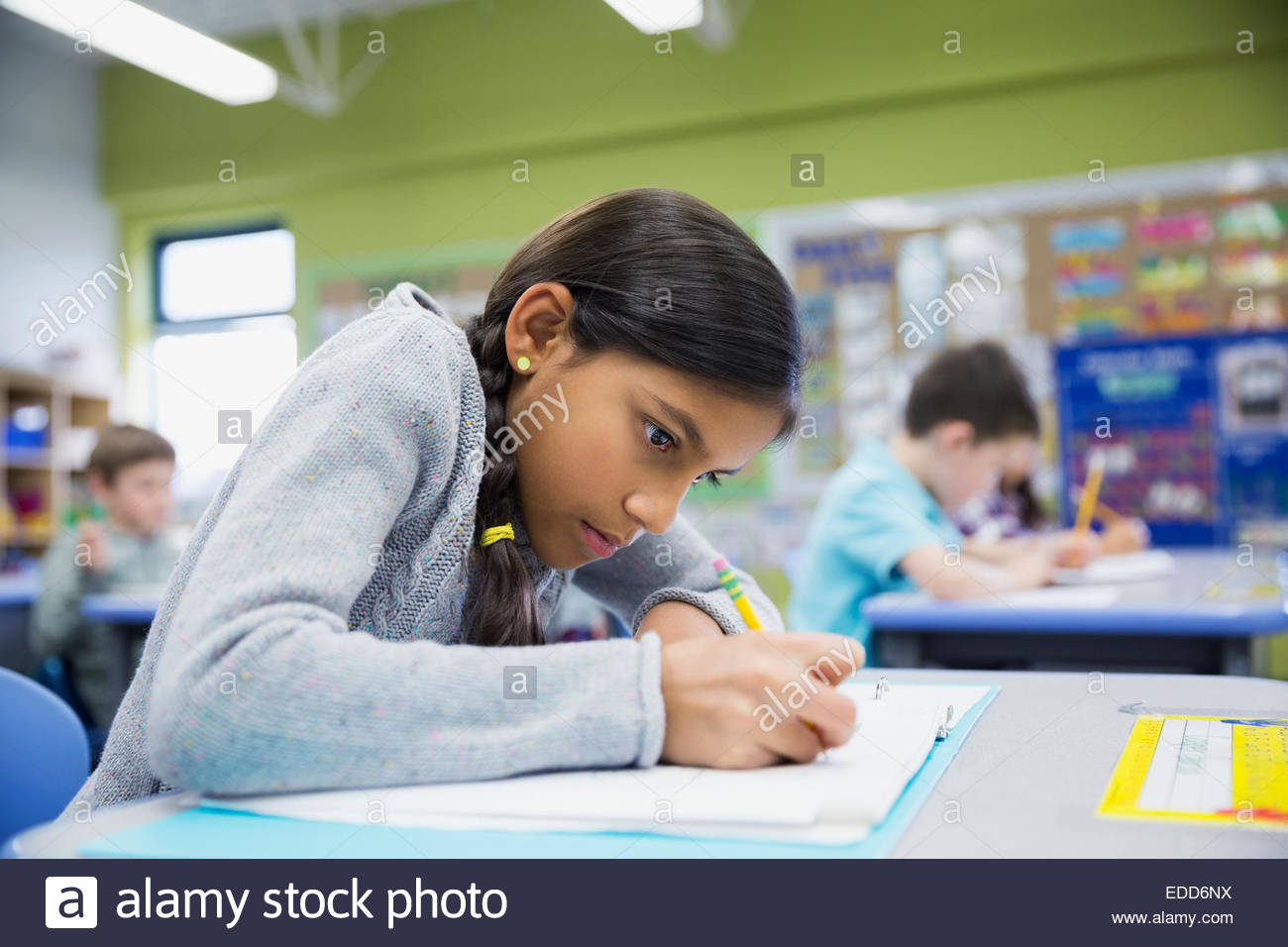 Focused elementary student writing at desk in classroom Stock Photo - Alamy
