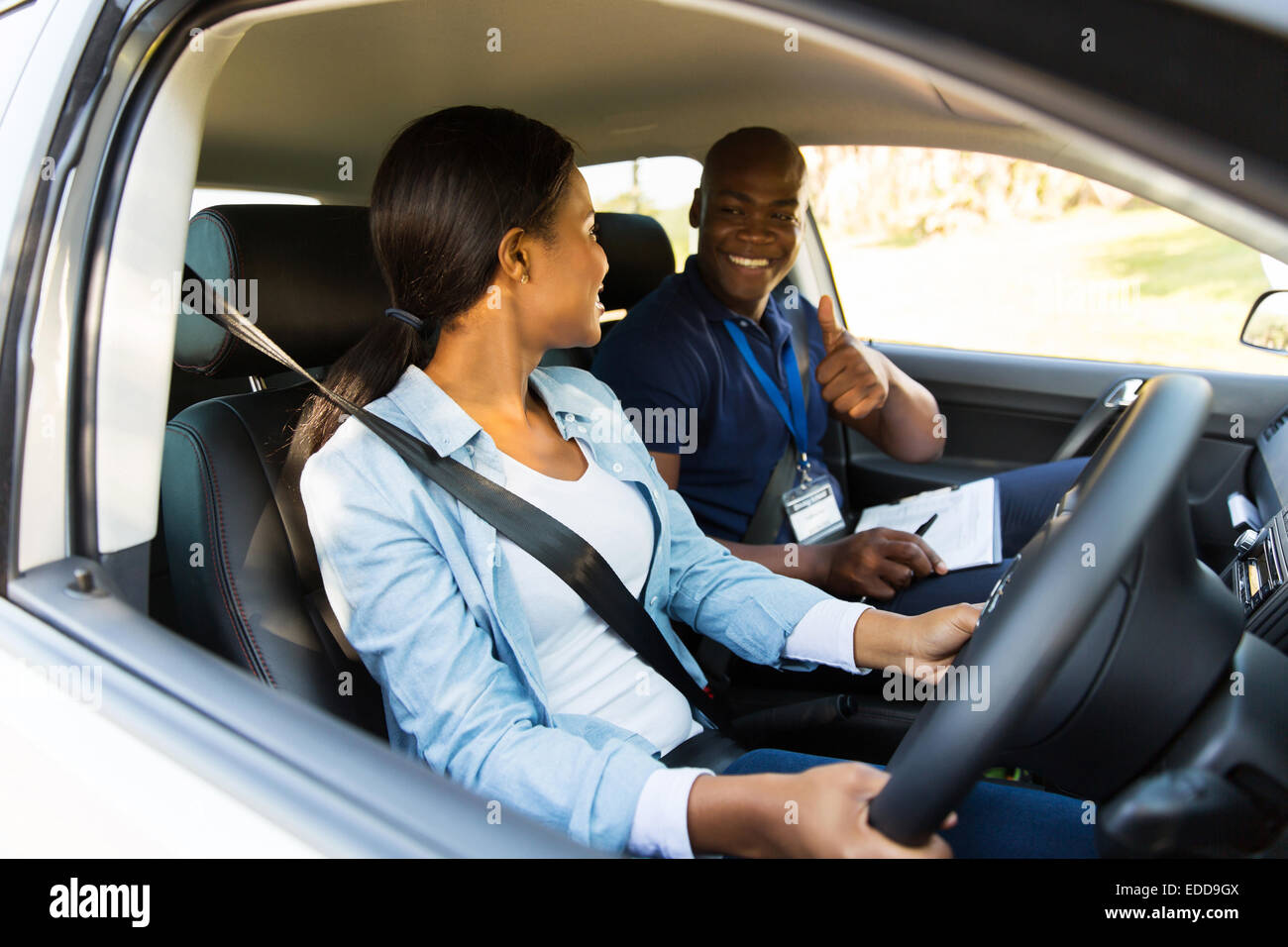smiling driving instructor giving thumbs up to learner driver during ...