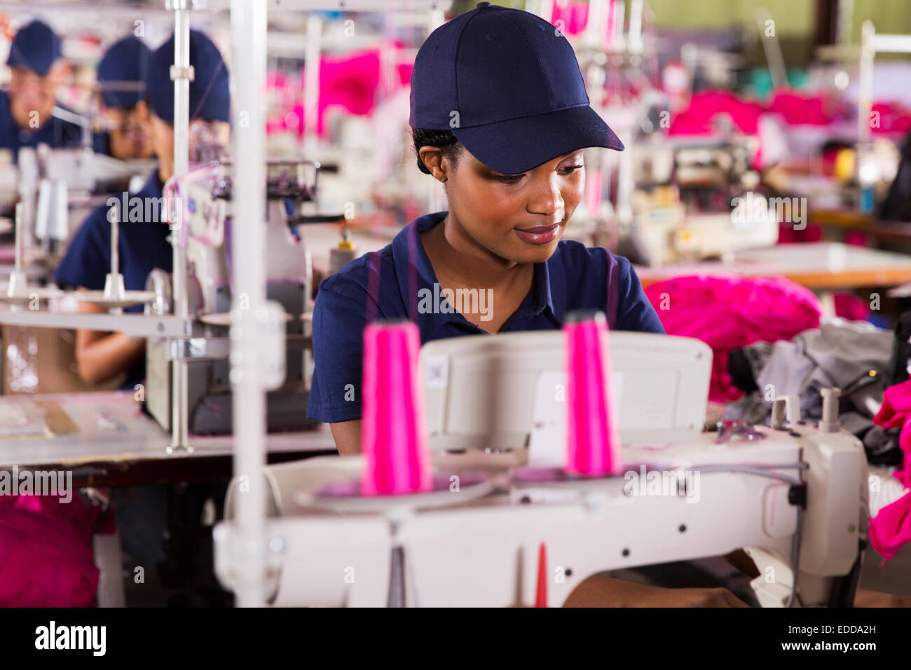 African clothing factory worker sewing with colleagues on background ...