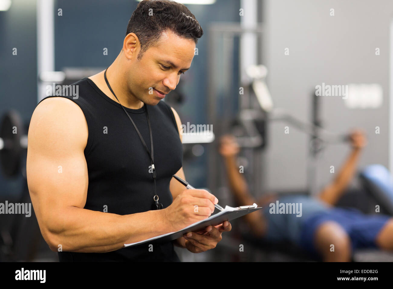 muscular mid age male gym trainer writing on clipboard Stock Photo - Alamy