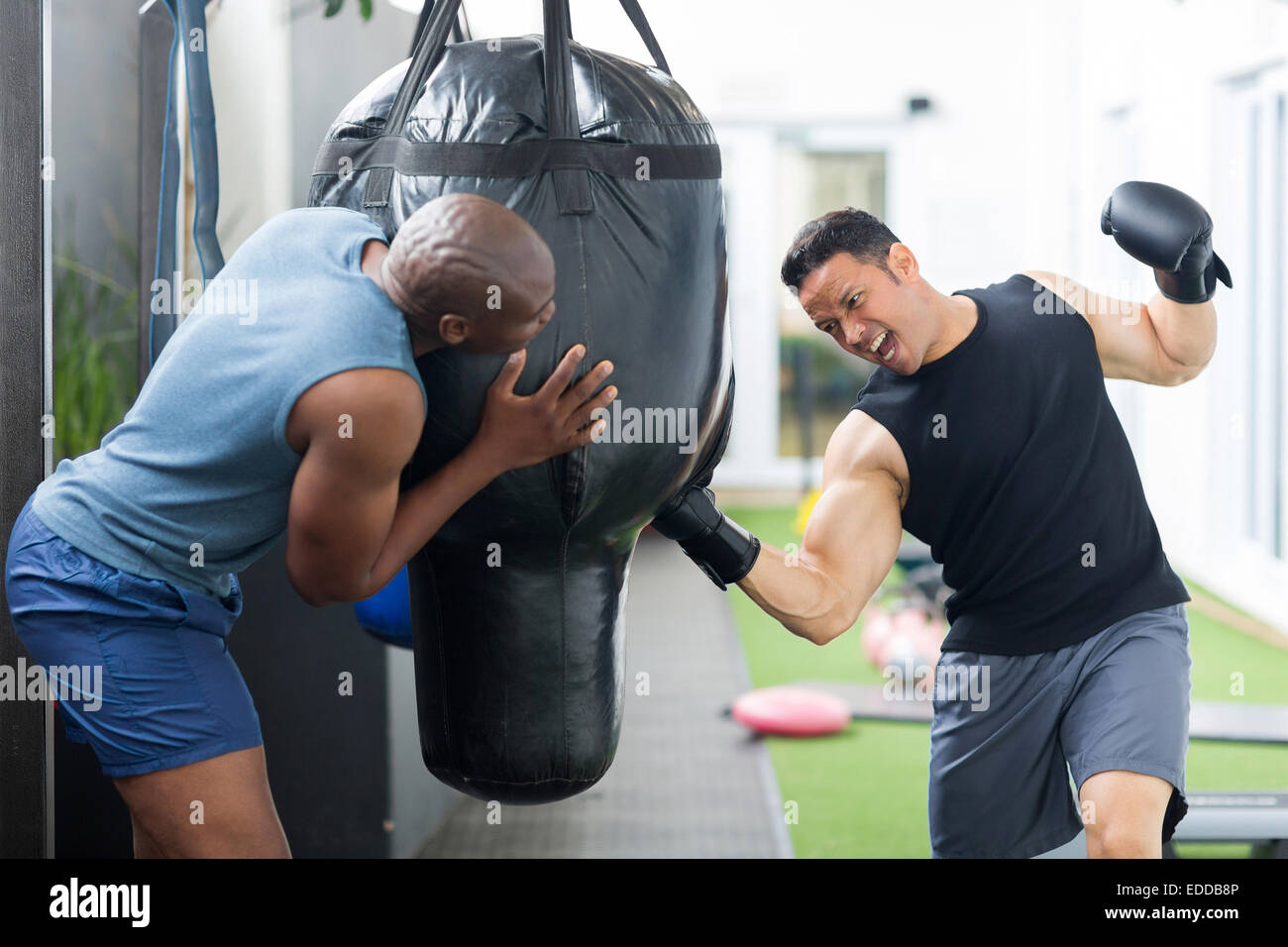 angry man training with punch bag in gym with personal trainer Stock ...