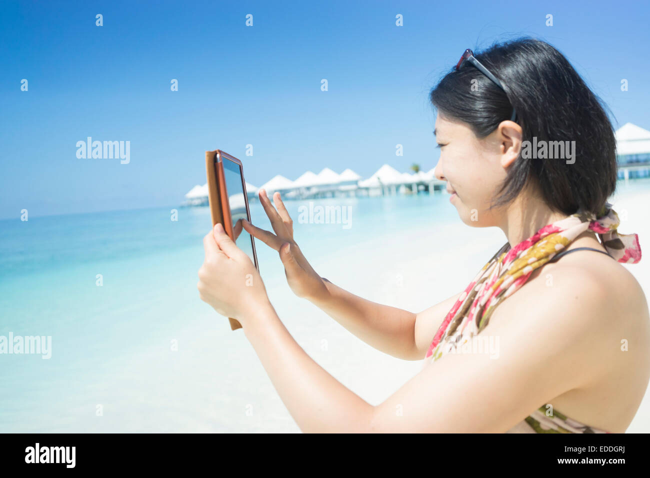 Maldives, Ari Atoll, young woman taking photograph with her mini tablet ...