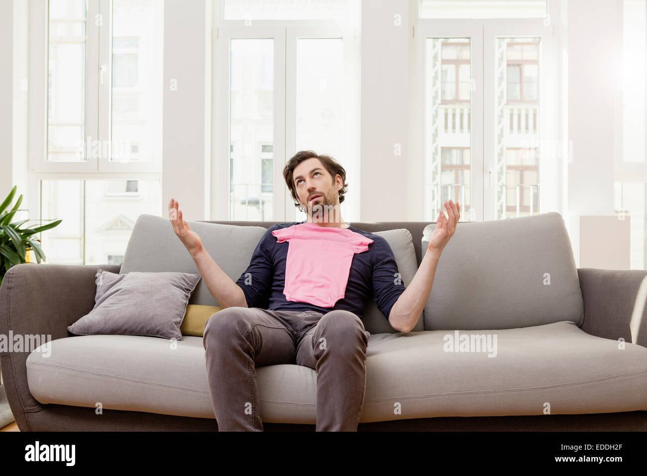 Disappointed man with pink baby shirt on couch Stock Photo - Alamy