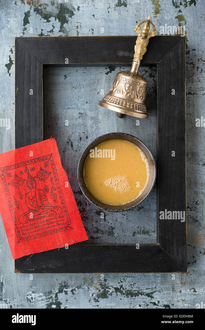 Bowl of butter tea, red prayer flag, black picture frame and bell on ...