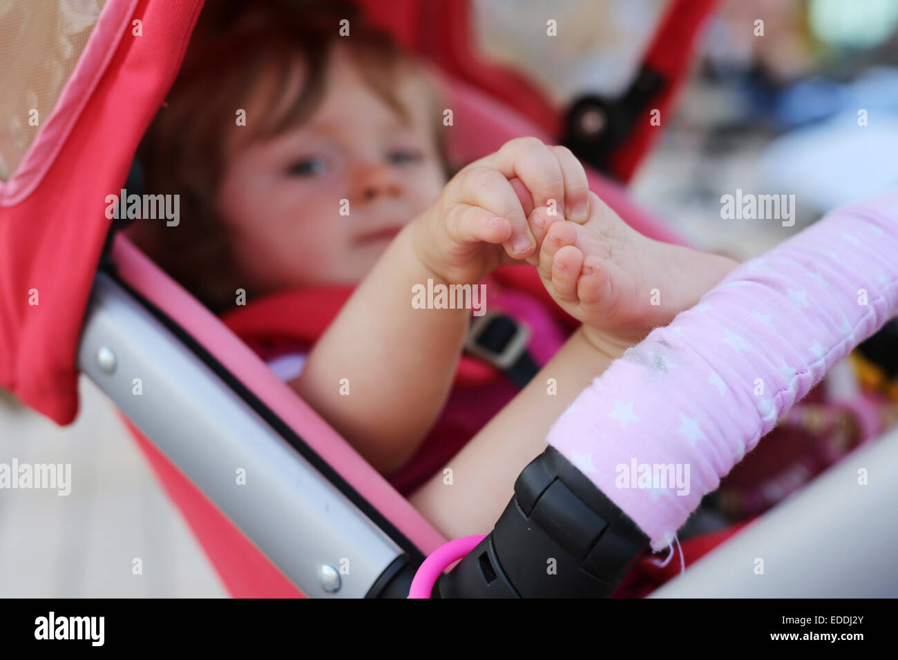 Little girl in baby buggy playing with her toes Stock Photo - Alamy