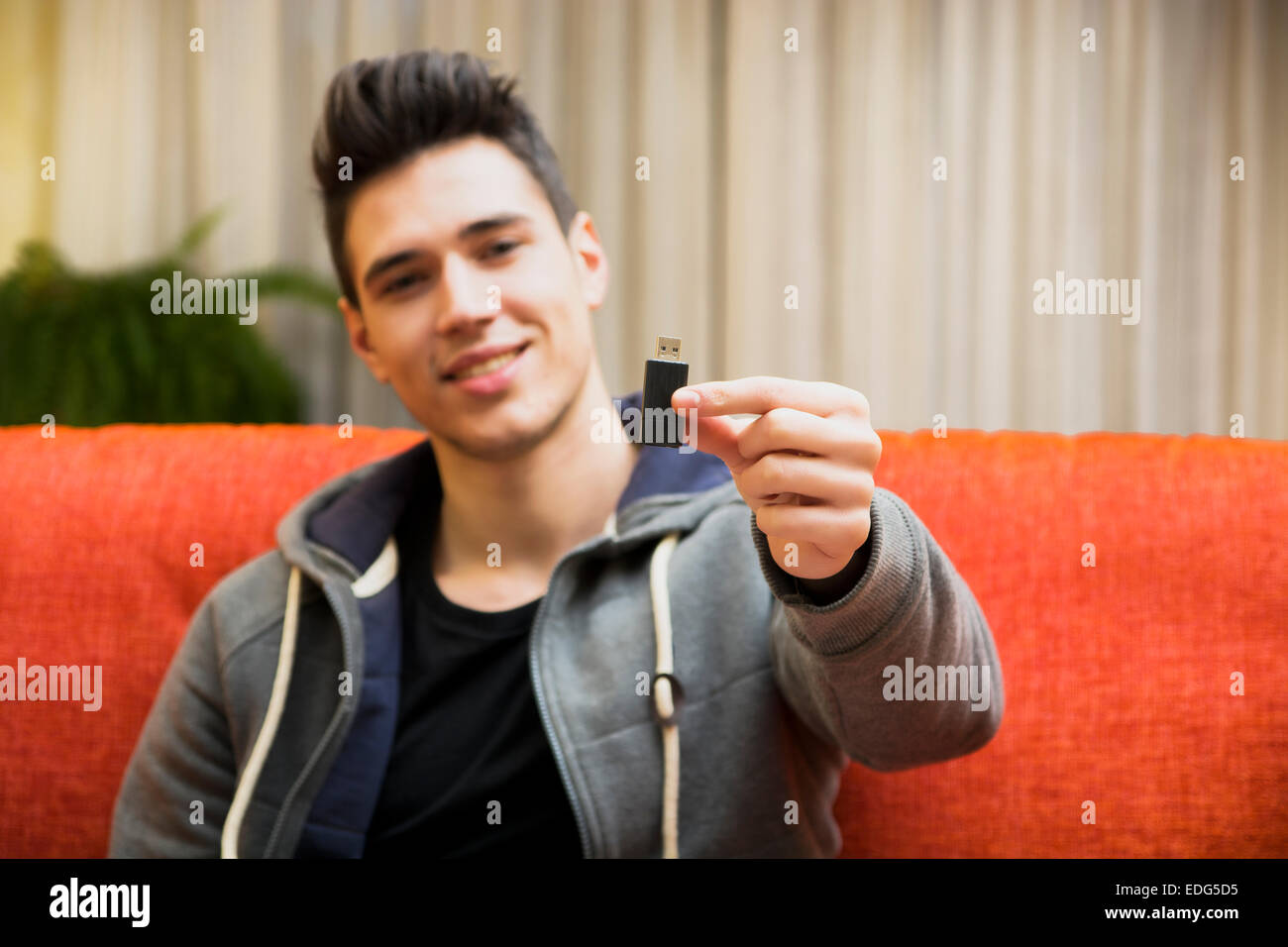 Handsome smiling young man at home showing USB key in his hand, sitting ...