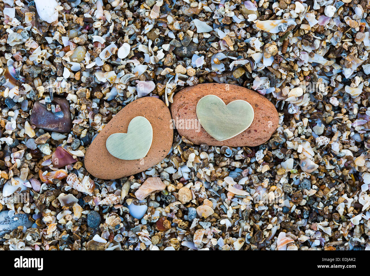 Two bright beautiful metal hearts are placed on two red rocks on sandy ...