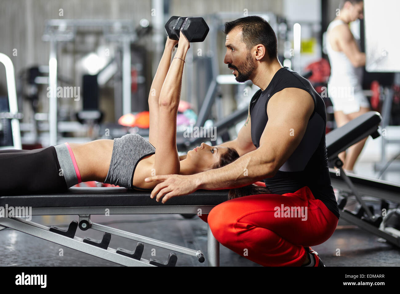 Personal fitness trainer assisting a young woman in the gym at a ...