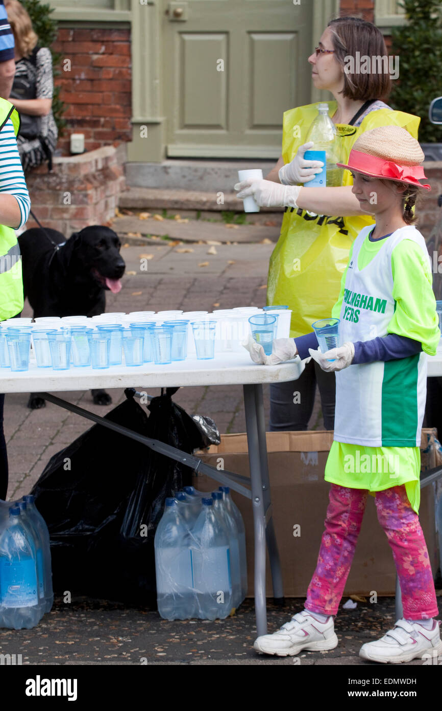 Women and a teenage girl in a straw hat run a water station handing up ...