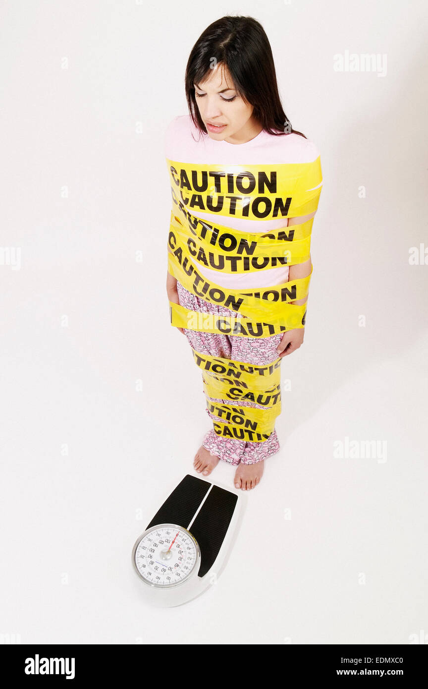 woman wrapping in caution tape in front of scale Stock Photo - Alamy