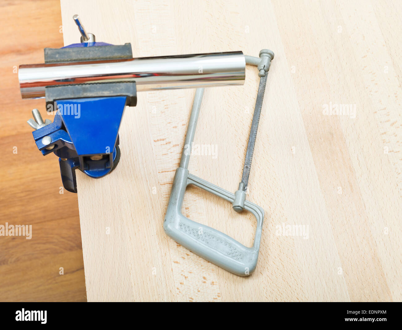 hacksaw and chrome plated plumbing drain pipe gripped in vice on wooden ...