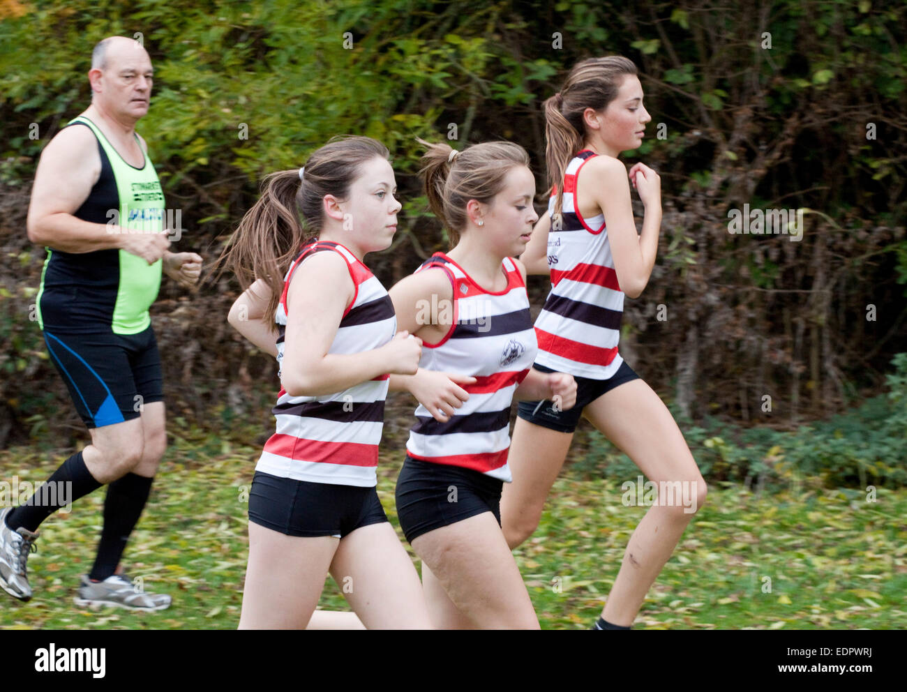 Three teenage girls in matching club vest compete in a cross country ...