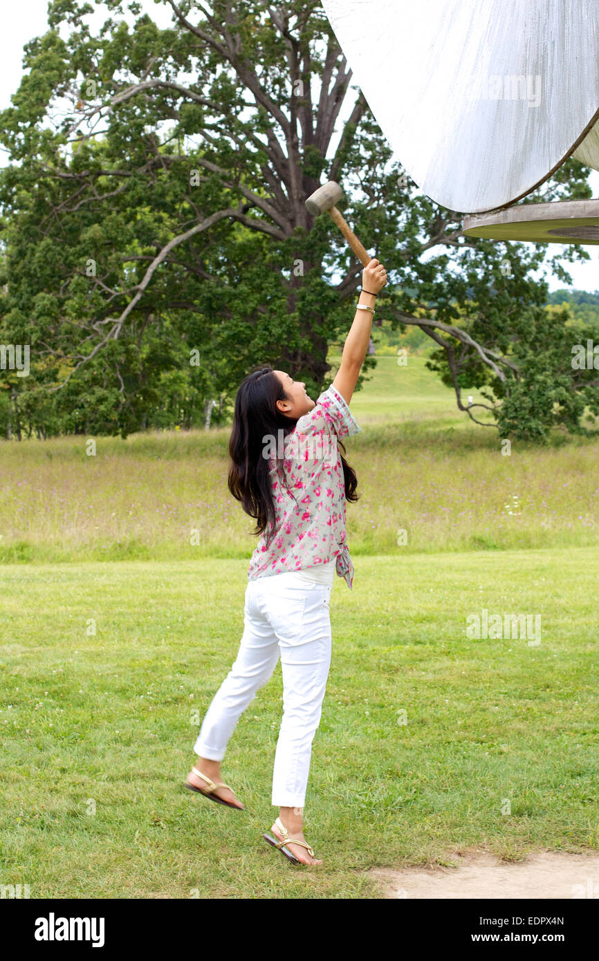 Beautiful young Asian woman jumps up to strike a giant gong with a ...