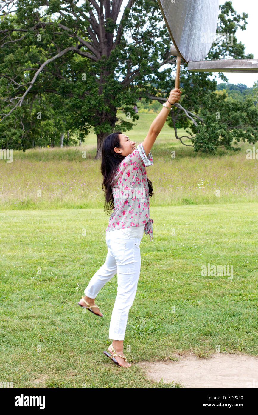 Beautiful young Asian woman jumps up to strike a giant gong with a ...