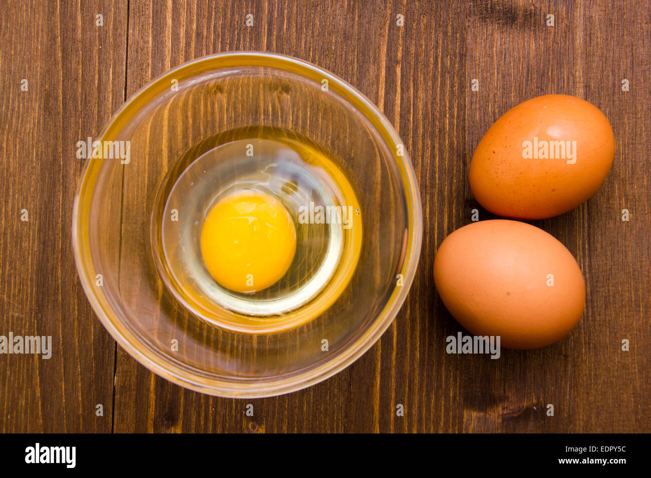 Open egg on bowl on wooden table seen from above Stock Photo - Alamy