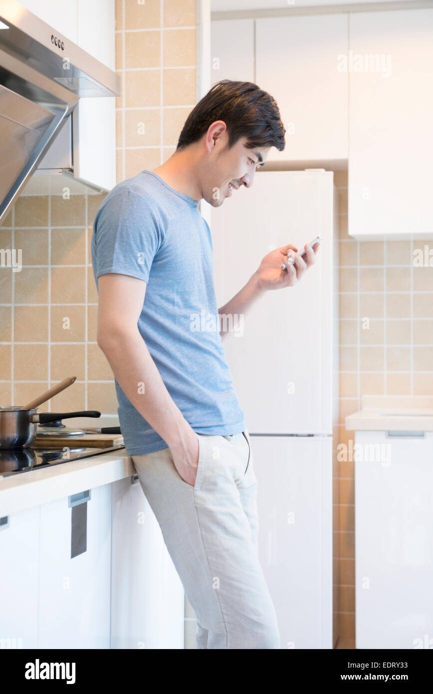 Young man using mobile in kitchen Stock Photo - Alamy