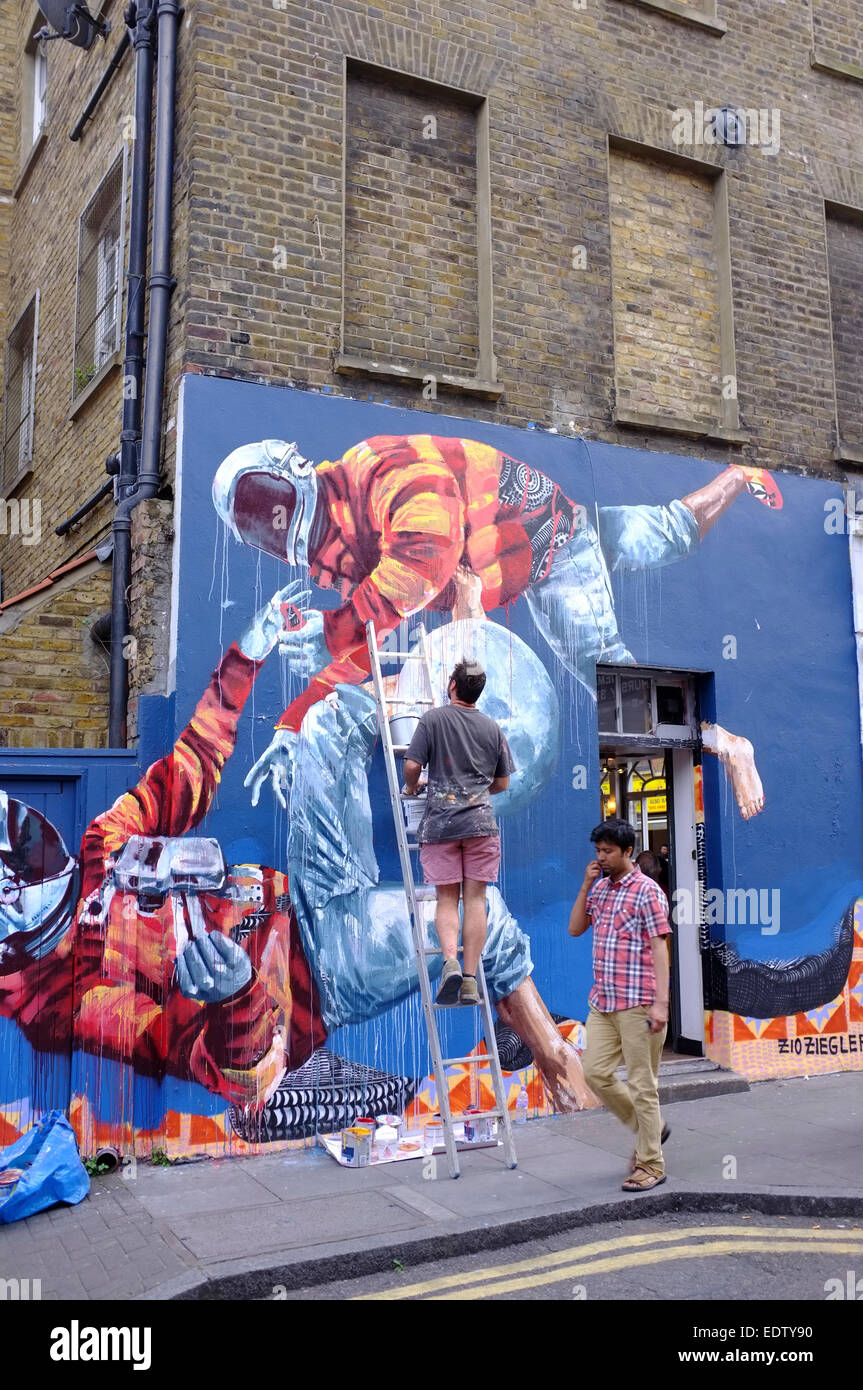 artist on a ladder painting art on a wall in Brick lane area of ...
