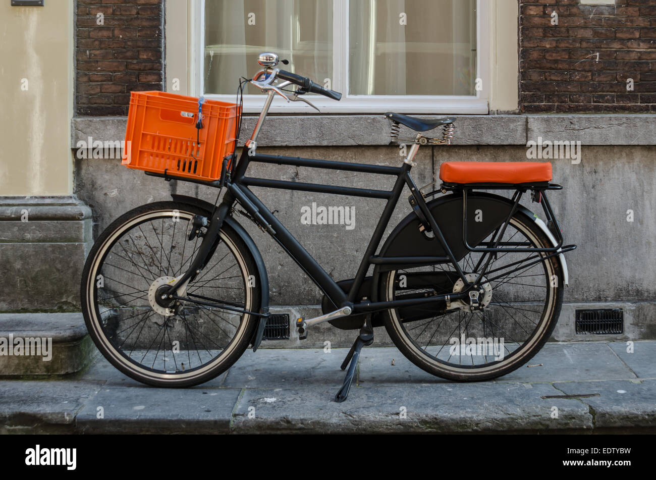 A vintage bicycle with orange accents is parked on a street sidewalk in ...