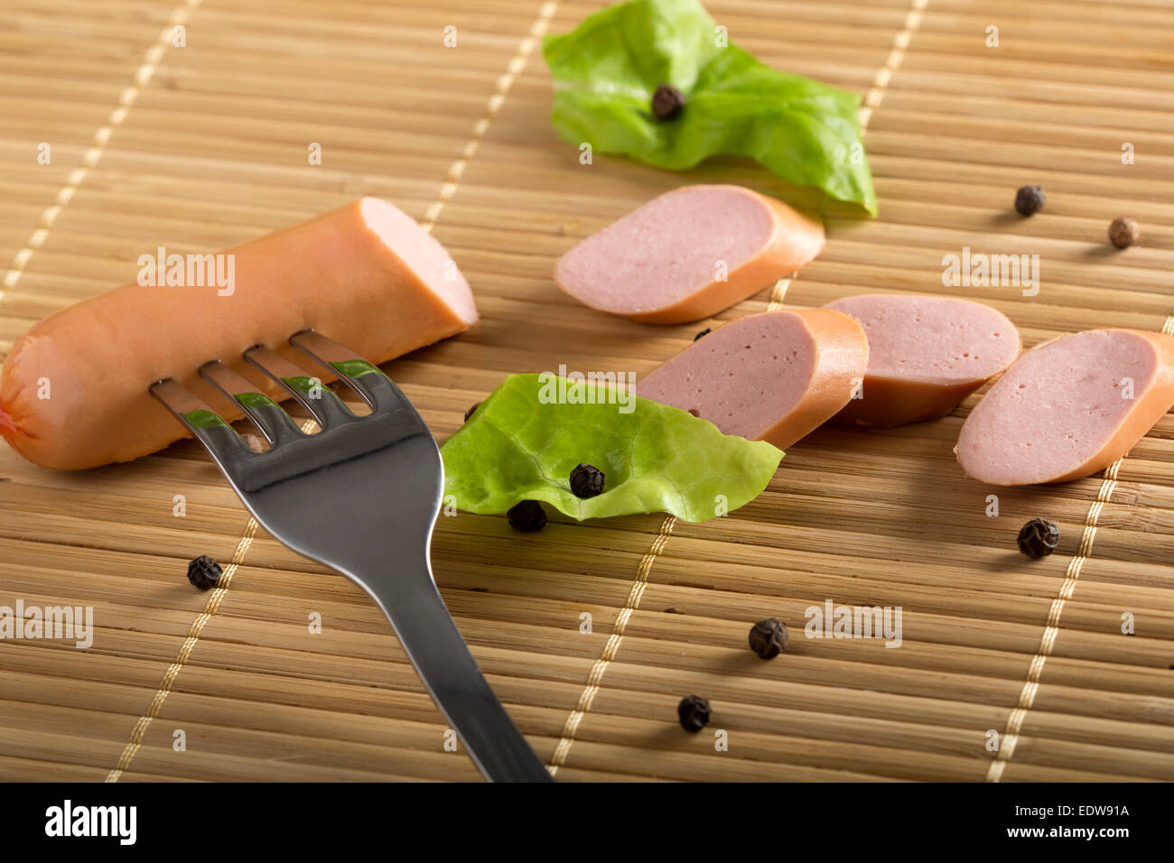 Sausage, prick with a fork and other slices over bamboo background ...