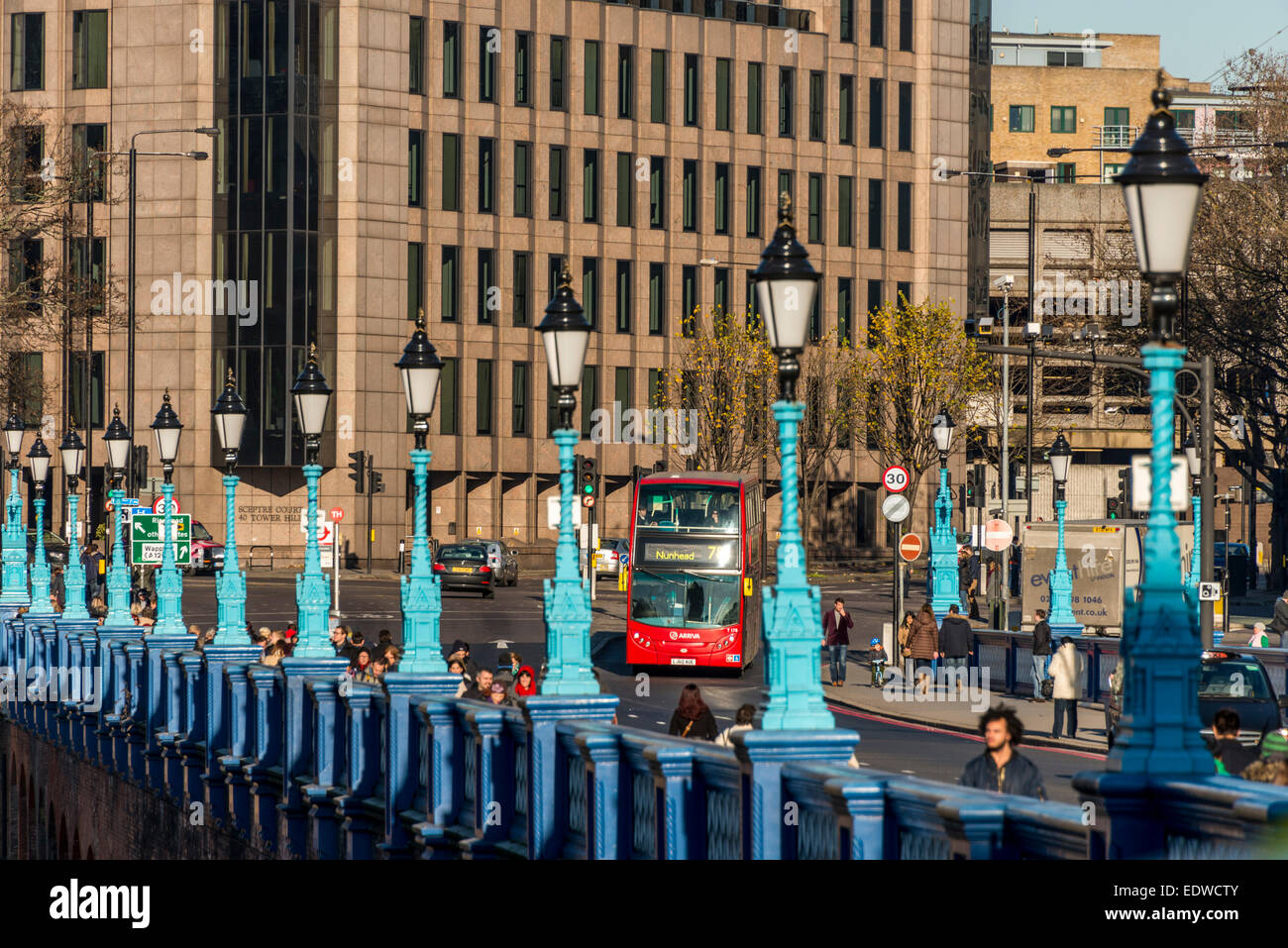 A London red bus entering Tower Bridge Approach, lined by streetlamps ...