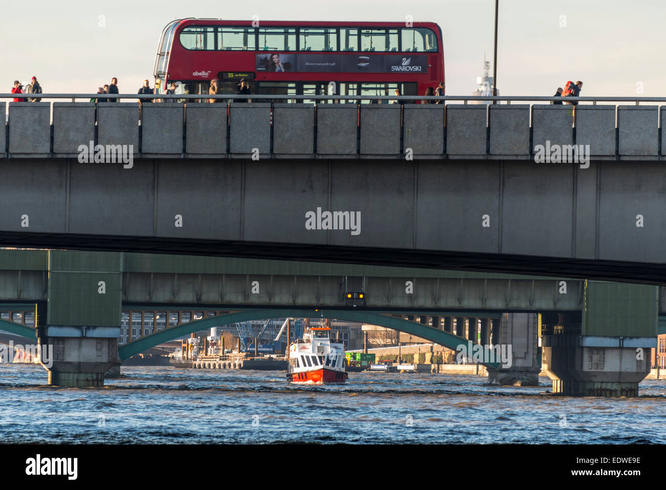 A London red bus passes over London Bridge while a River Thames cruise ...