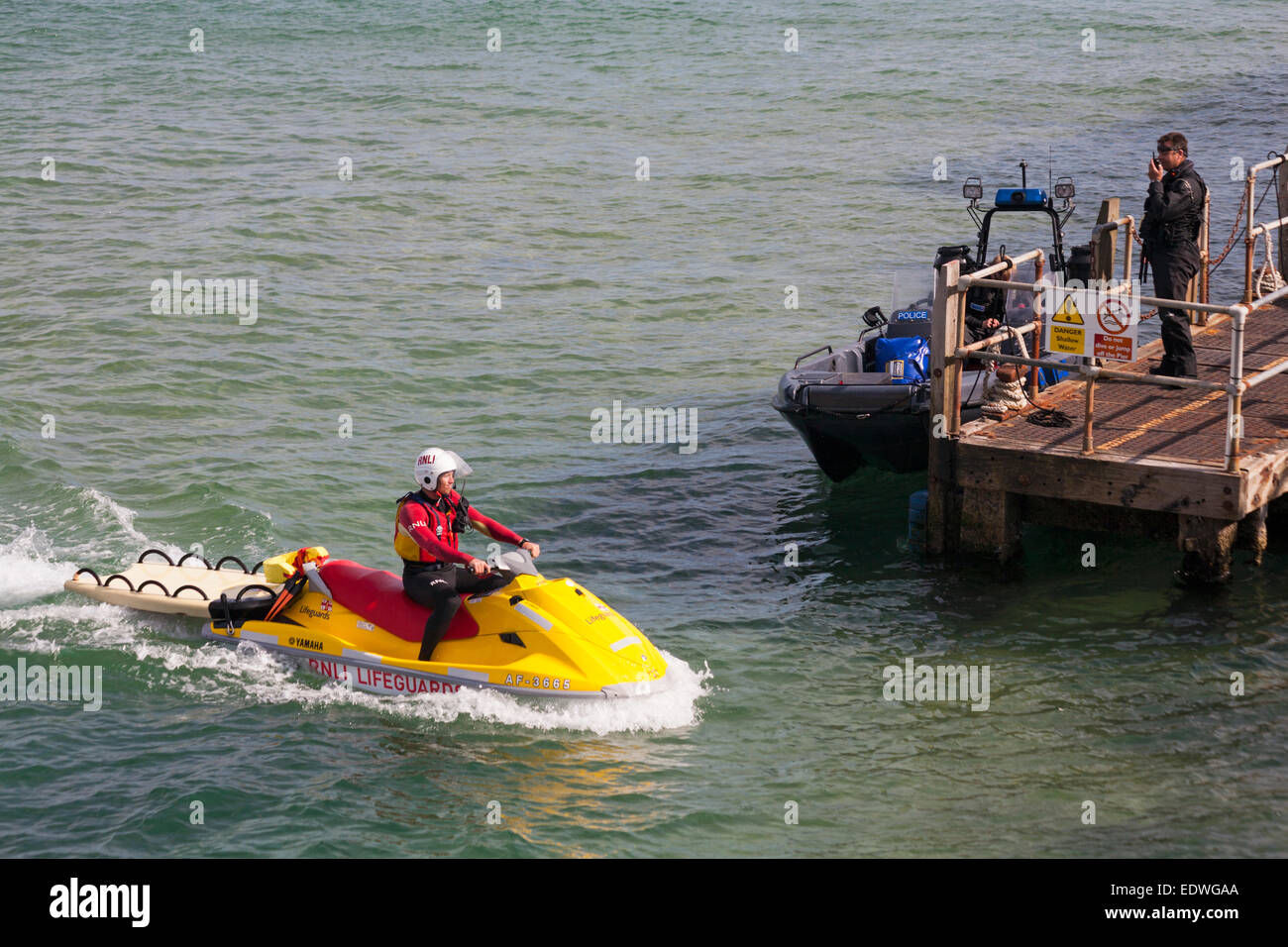 RNLI Lifeguards jetski with lifeguard approaching pier where police on ...