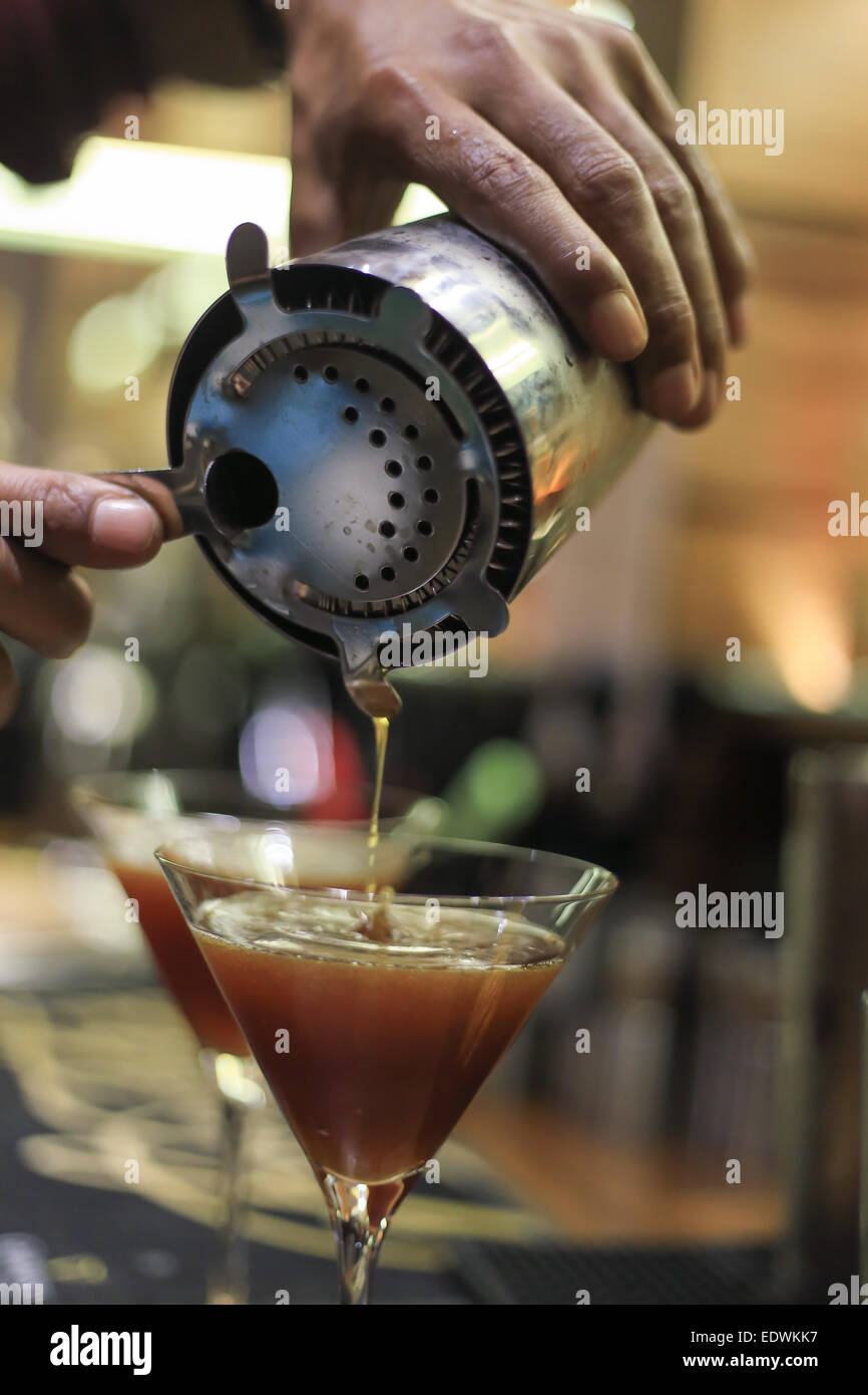 Hand pouring a cocktail from the mixing jug to the glass with liquid in ...
