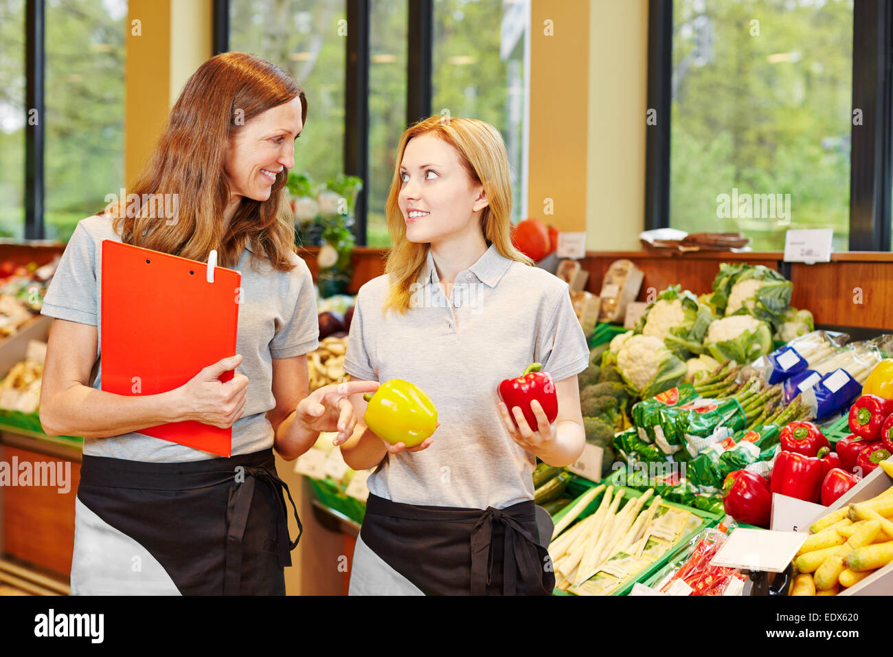 Store manager in supermarket teaching trainee in the vegetables section ...