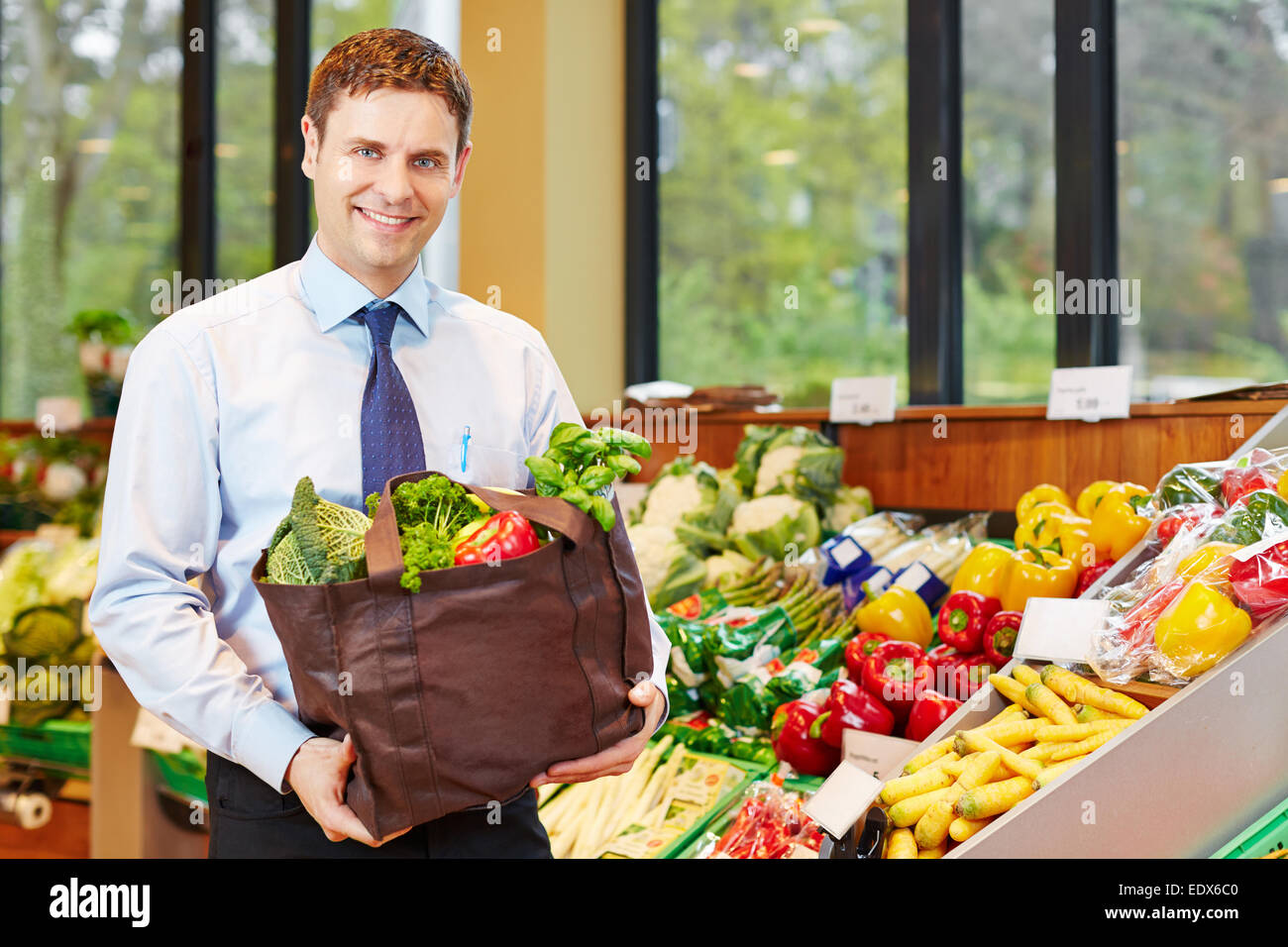 Smiling businessman buying bag of fresh vegetables in organic food ...