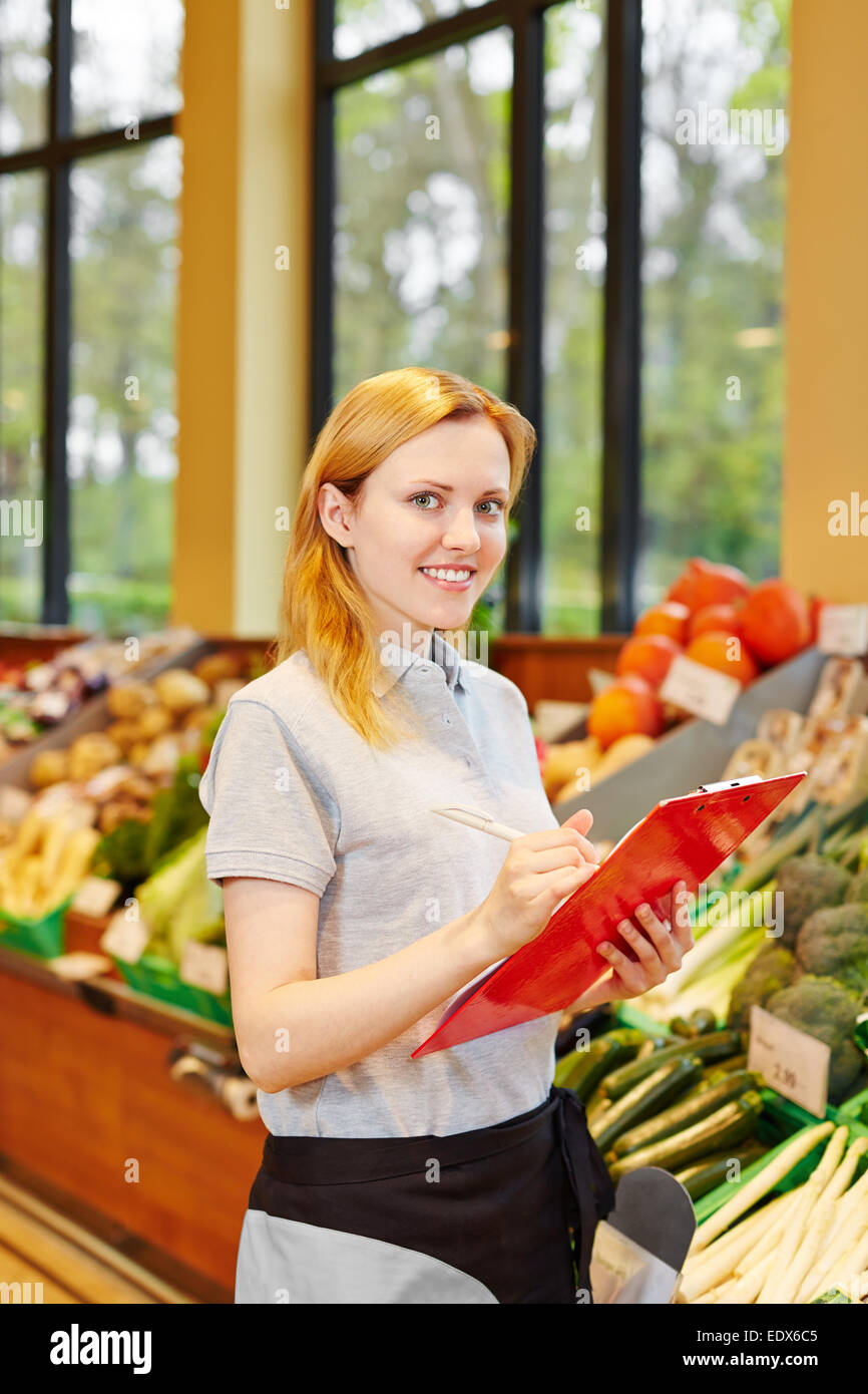 Smiling young woman as salesperson with clipboard in supermarkt Stock ...