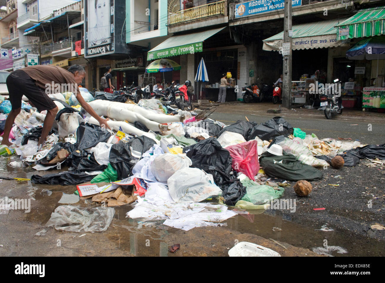 A man reaches for a mannequin leg in a large pile of garbage on a city ...