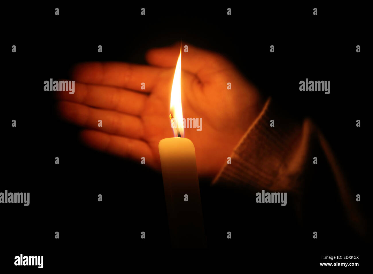 hand protects the flame from a candle burning on a dark background ...