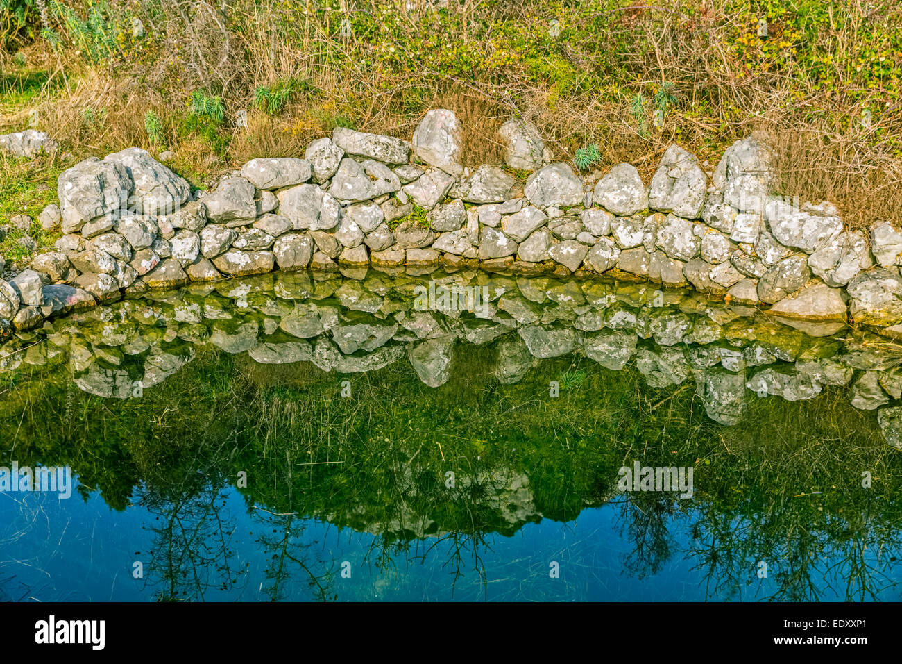 Ancient water trough with surrounding nature reflecting in the water at ...