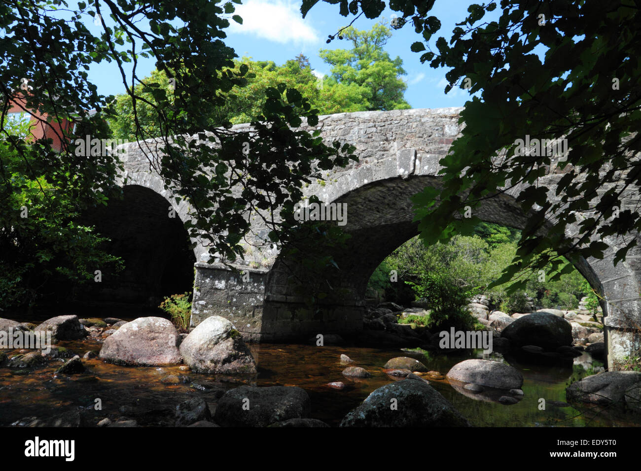 An 18th century grey stone bridge over a brown moorland stream strewn ...