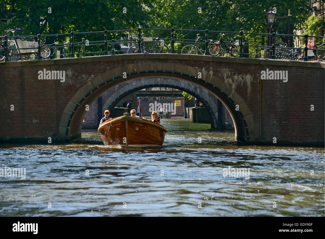 Wooden boat passing beneath an a canal bridge, Amsterdam, North Holland ...