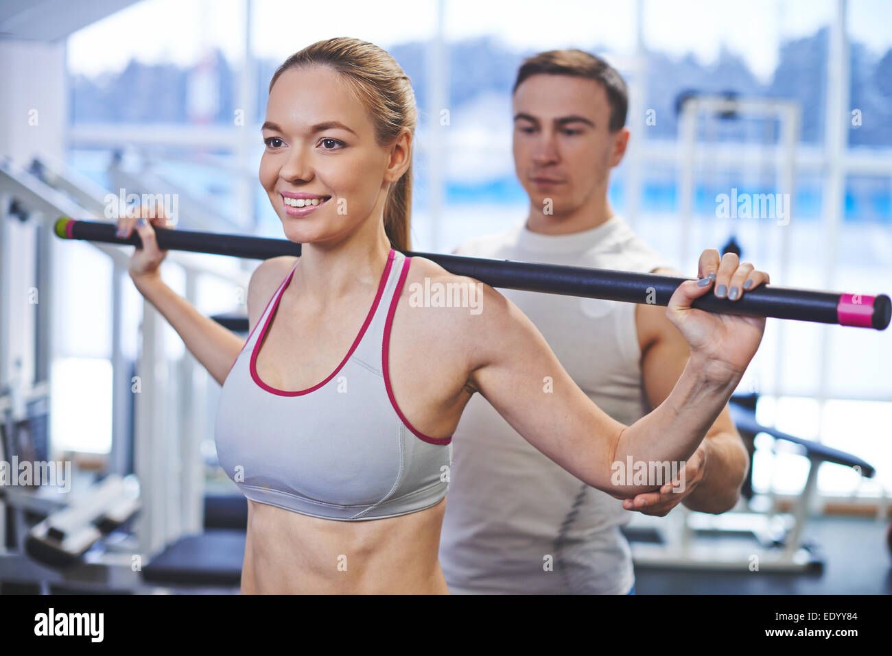 Portrait of pretty girl weightlifting in gym, her trainer helping her ...