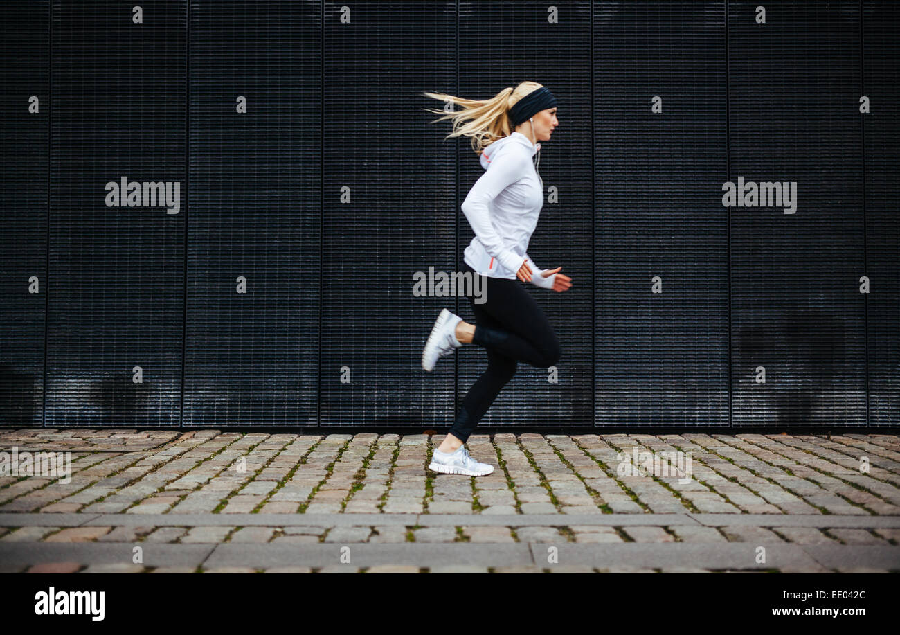 Side view of sporty young woman running on sidewalk in morning. Health ...